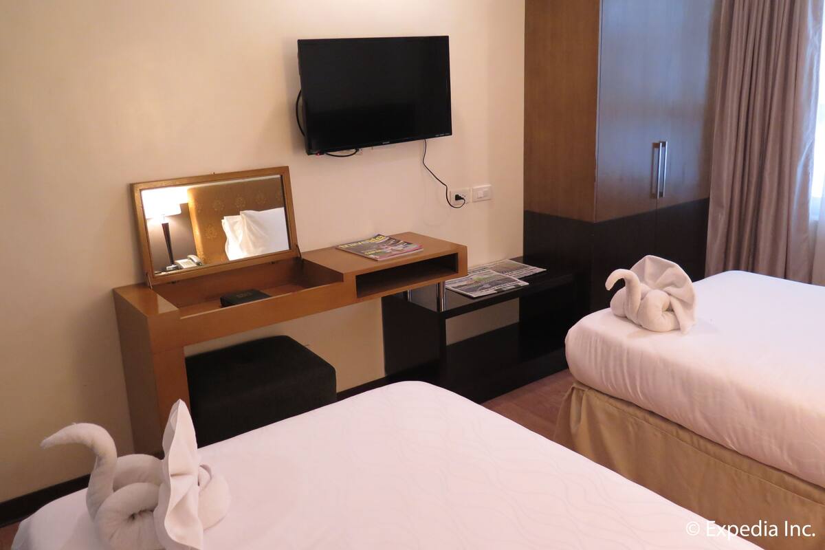 Quarto de hotel com escrivaninha, televisão, guarda-roupa e duas camas.