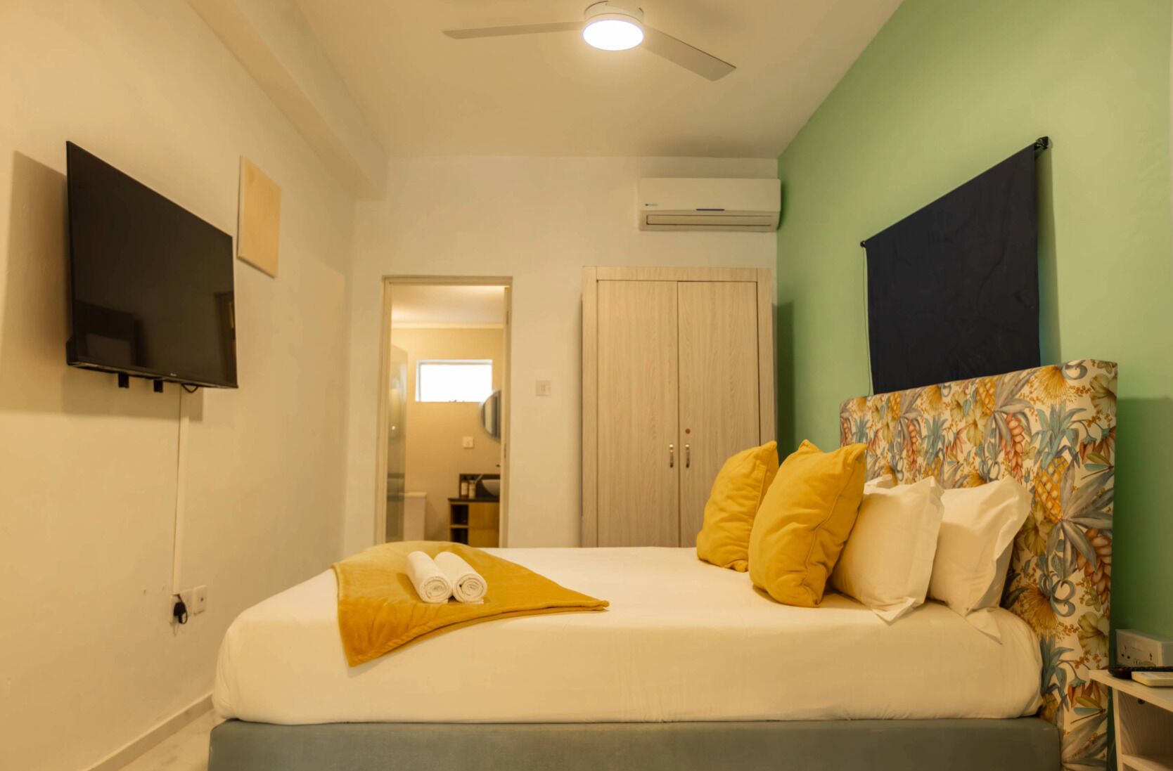 Quarto com uma cama, televisão fixada na parede e ar condicionado.