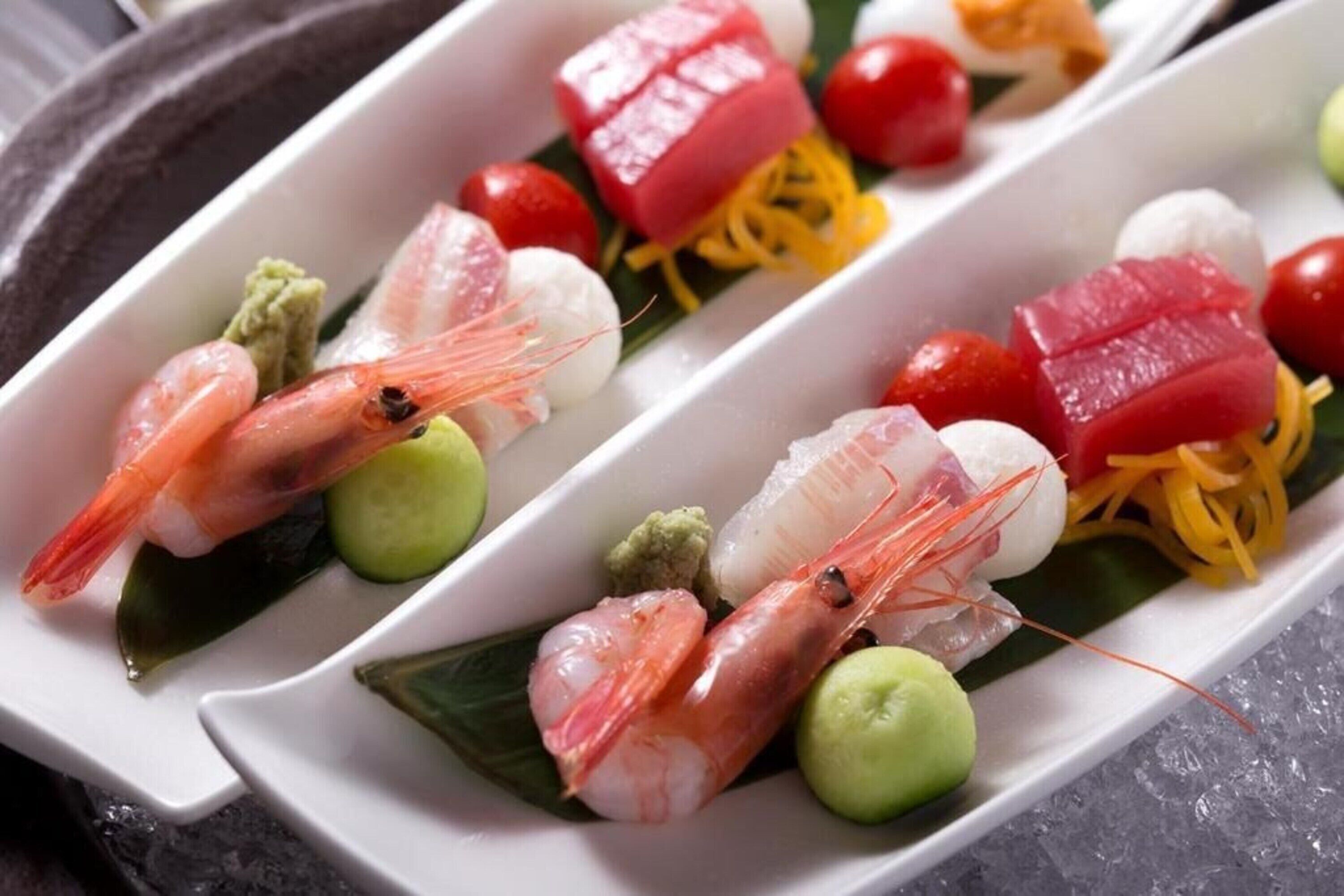 Variedade de sushi e sashimi sobre um prato retangular branco com gelo.