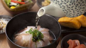 Uma tigela de sashimi com um enfeite verde, um bule de chá e um pequeno recipiente de wasabi.