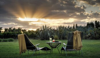 Vista do pôr do sol com duas cadeiras e uma mesa numa área gramada.