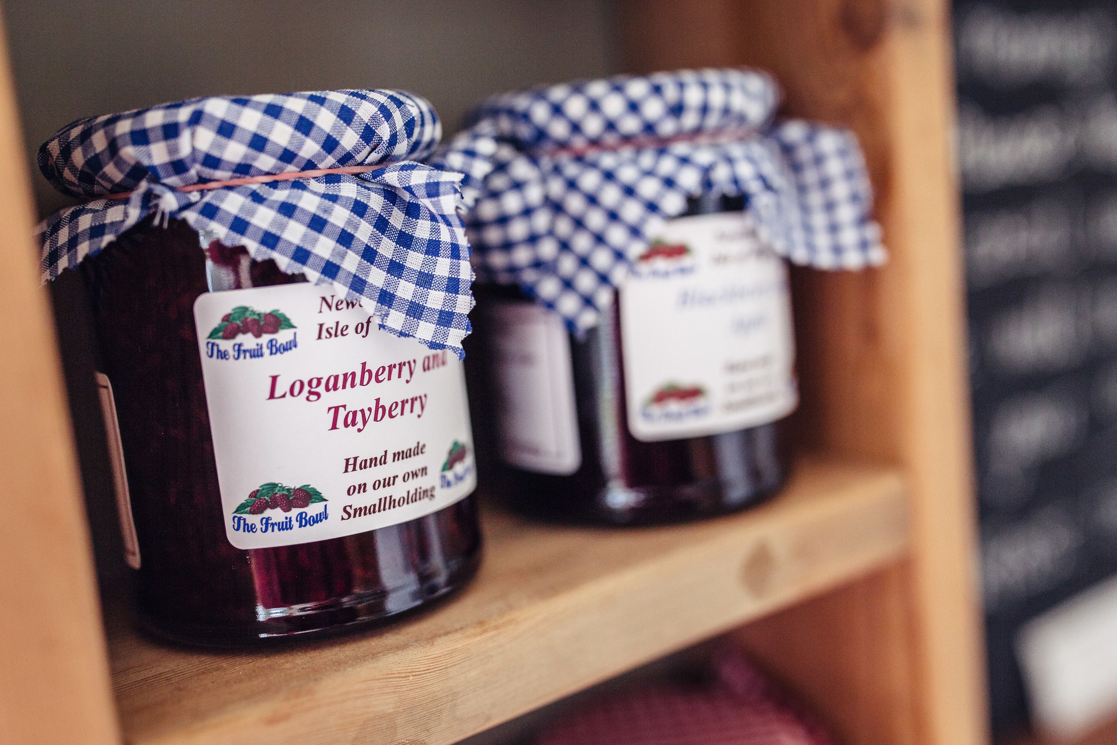 Potes de geleia de loganberry e tayberry sobre uma prateleira de madeira.