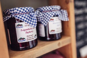 Potes de geleia de loganberry e tayberry sobre uma prateleira de madeira.
