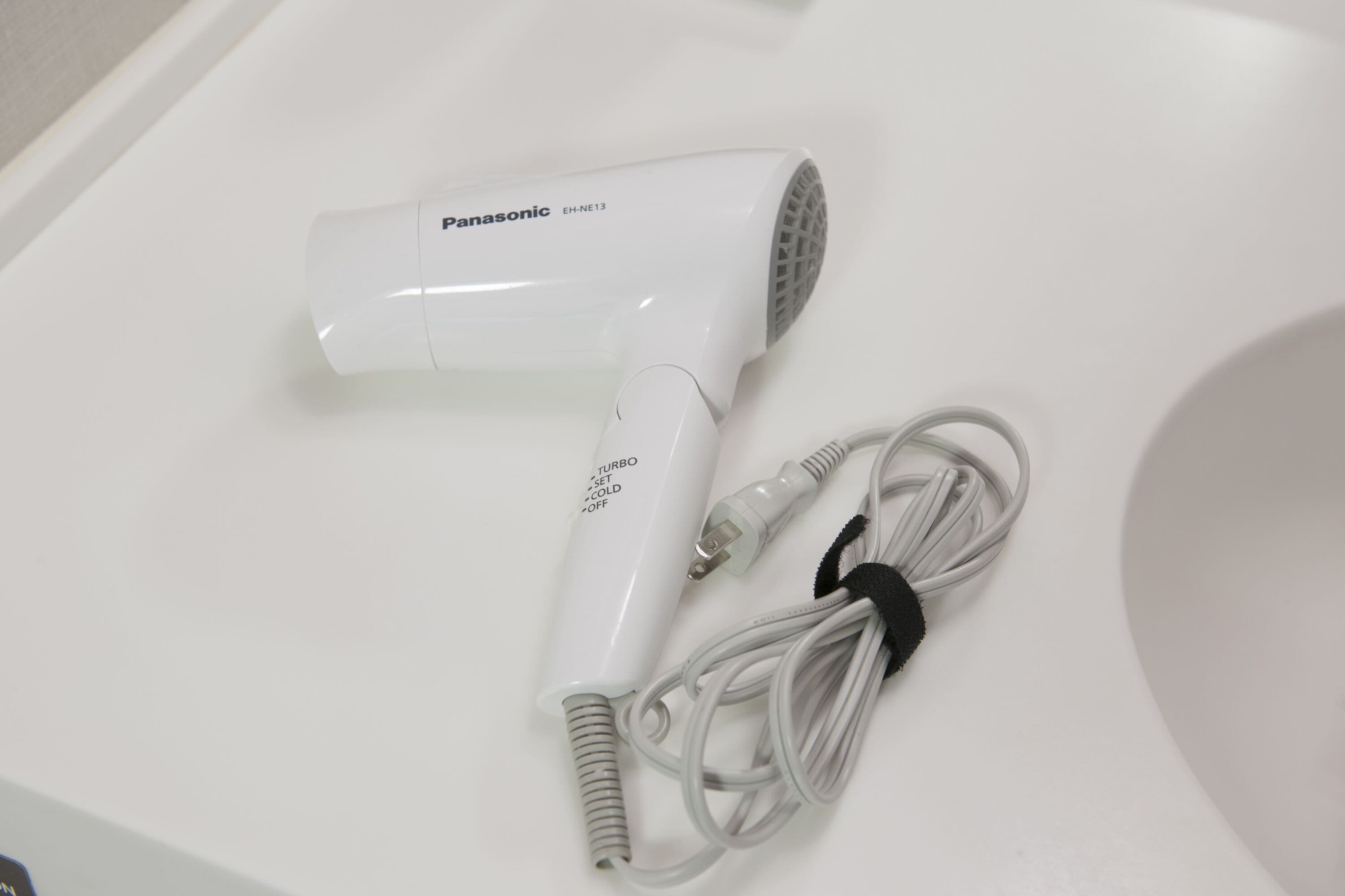 Um secador de cabelo Panasonic com fio e adaptador de energia sobre uma superfície branca.