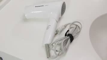 Um secador de cabelo Panasonic com fio e adaptador de energia sobre uma superfície branca.