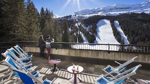 Terraço com cadeiras de descanso e uma mesa, com vista para uma paisagem montanhosa coberta de neve.