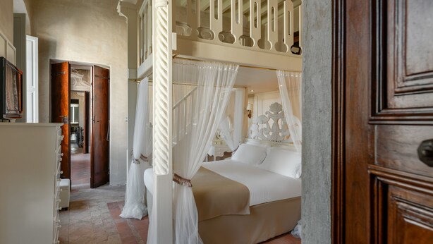 Quarto com cama de dossel, porta de madeira e corredor que dá para outros aposentos.
