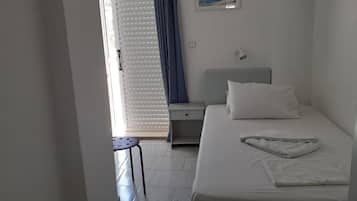 Quarto com cama, mesa de cabeceira, cadeira e janela com persianas.