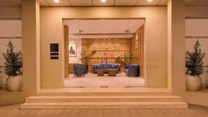 Um hall de entrada com balcão de recepção, área de estar com sofás e poltronas, e plantas em vasos.