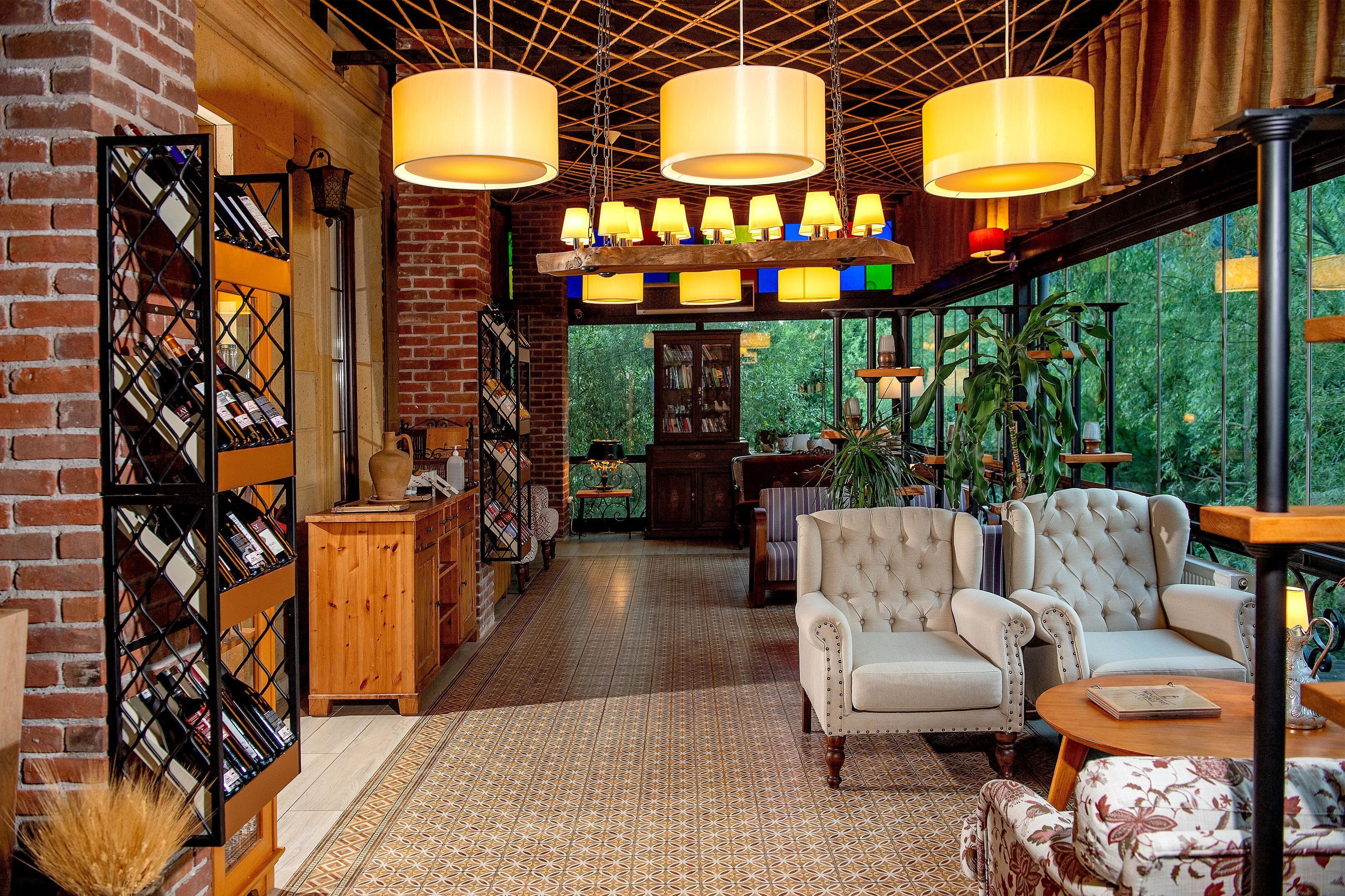 Um interior acolhedor com parede de tijolos, espaço para vinhos, assentos confortáveis e grandes janelas com vista para o verde.