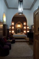 Quarto com uma cama grande, uma televisão e um espaço de estar com pufes.