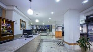 Uma área de recepção de hotel com piso de mármore, balcão de atendimento, espelho e planta em vaso.