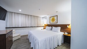 Quarto de hotel com uma cama grande, uma escrivaninha, uma cadeira e um quadro na parede.