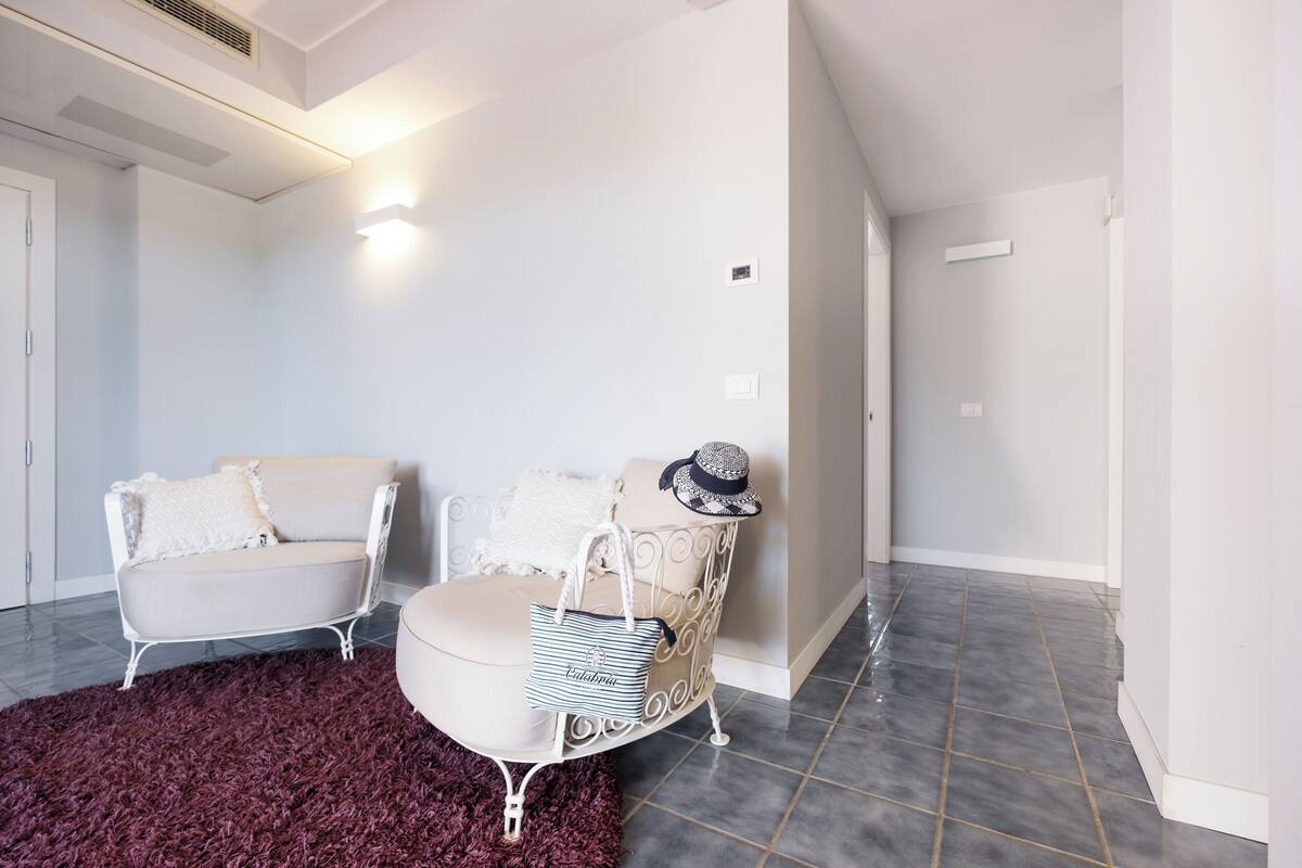 Uma sala de estar moderna com um sofá branco, uma poltrona estampada e um chapéu decorativo no apoio de braço.