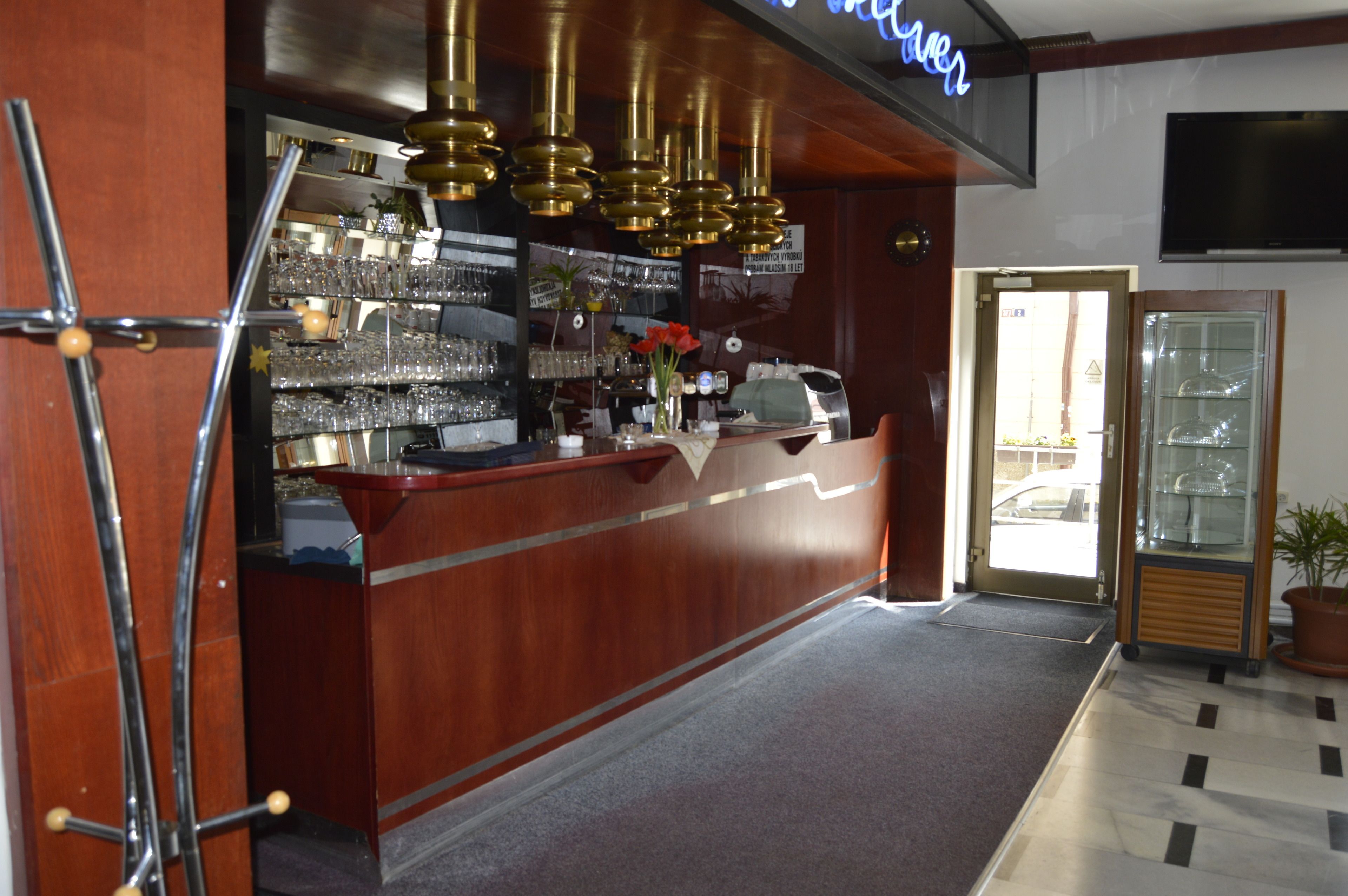 Uma área de bar com balcão de madeira, luminárias douradas pendentes e uma vitrine de vidro.
