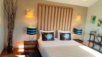 Quarto com cama, duas luminárias de cabeceira, mesa de apoio, um vaso com galhos e uma pequena mesa com objetos decorativos.