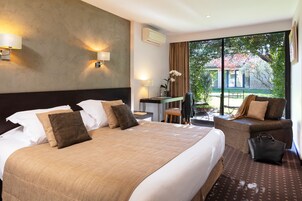 Quarto de hotel com uma cama grande, uma escrivaninha, uma cadeira e vista para o exterior.