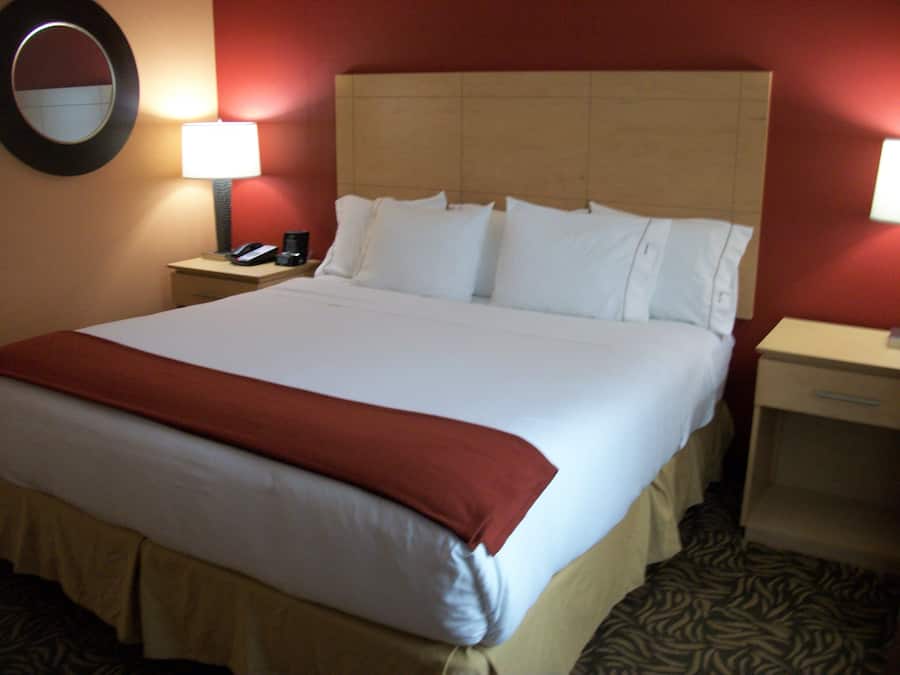 Quarto de hotel com cama grande, duas mesas de cabeceira, abajur e espelho na parede.