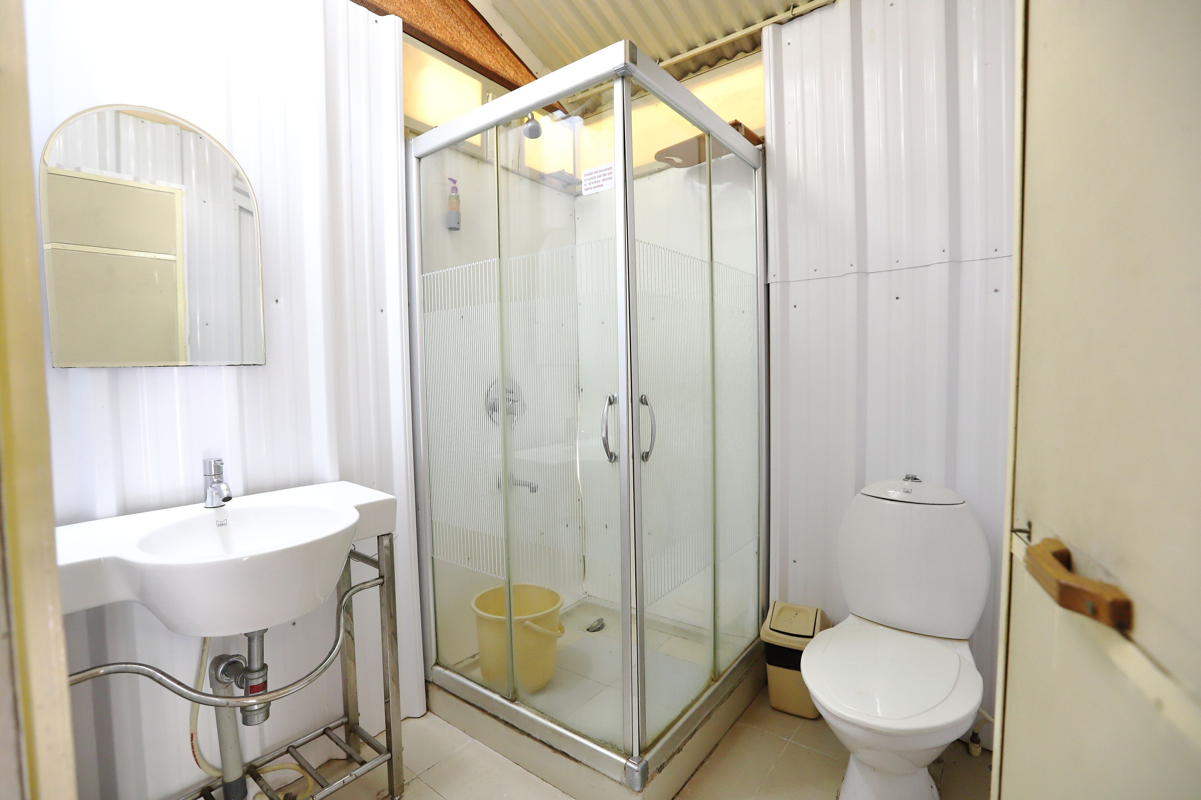 Casa de banho com chuveiro envolto em vidro, lavatório branco e sanita.