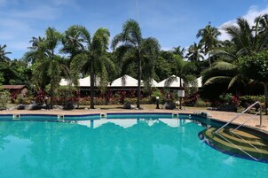 Piscina cercada por palmeiras e um deck revestido com azulejos.