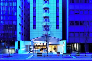 Um edifício moderno com entrada curva, grandes janelas e uma árvore em frente.