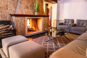 Uma sala de estar acolhedora com lareira de pedra, assentos confortáveis e uma mesa de centro com taças de vinho.