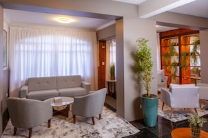Uma sala de estar moderna com um sofá cinzento, duas poltronas, uma mesa de centro e uma grande planta em vaso.