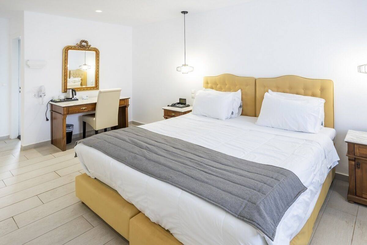 Quarto de hotel com cama grande, escrivaninha com cadeira, espelho e mesa de cabeceira.