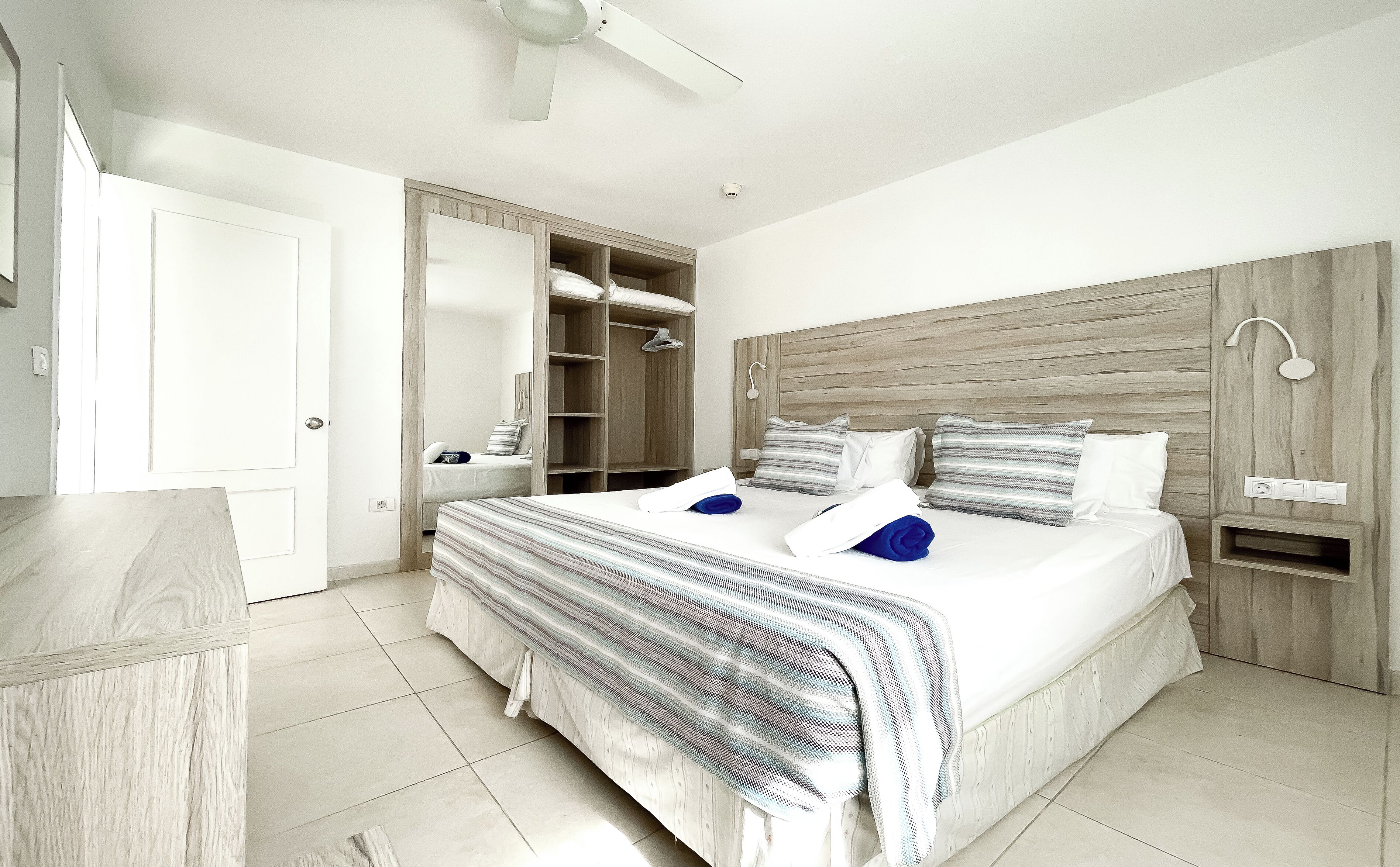 Quarto com cama grande, guarda-roupa, mesa de cabeceira e ventoinha no teto.