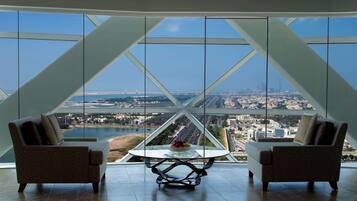 Um interior moderno com duas poltronas, uma mesa de vidro e vista para a paisagem urbana através de amplas janelas.