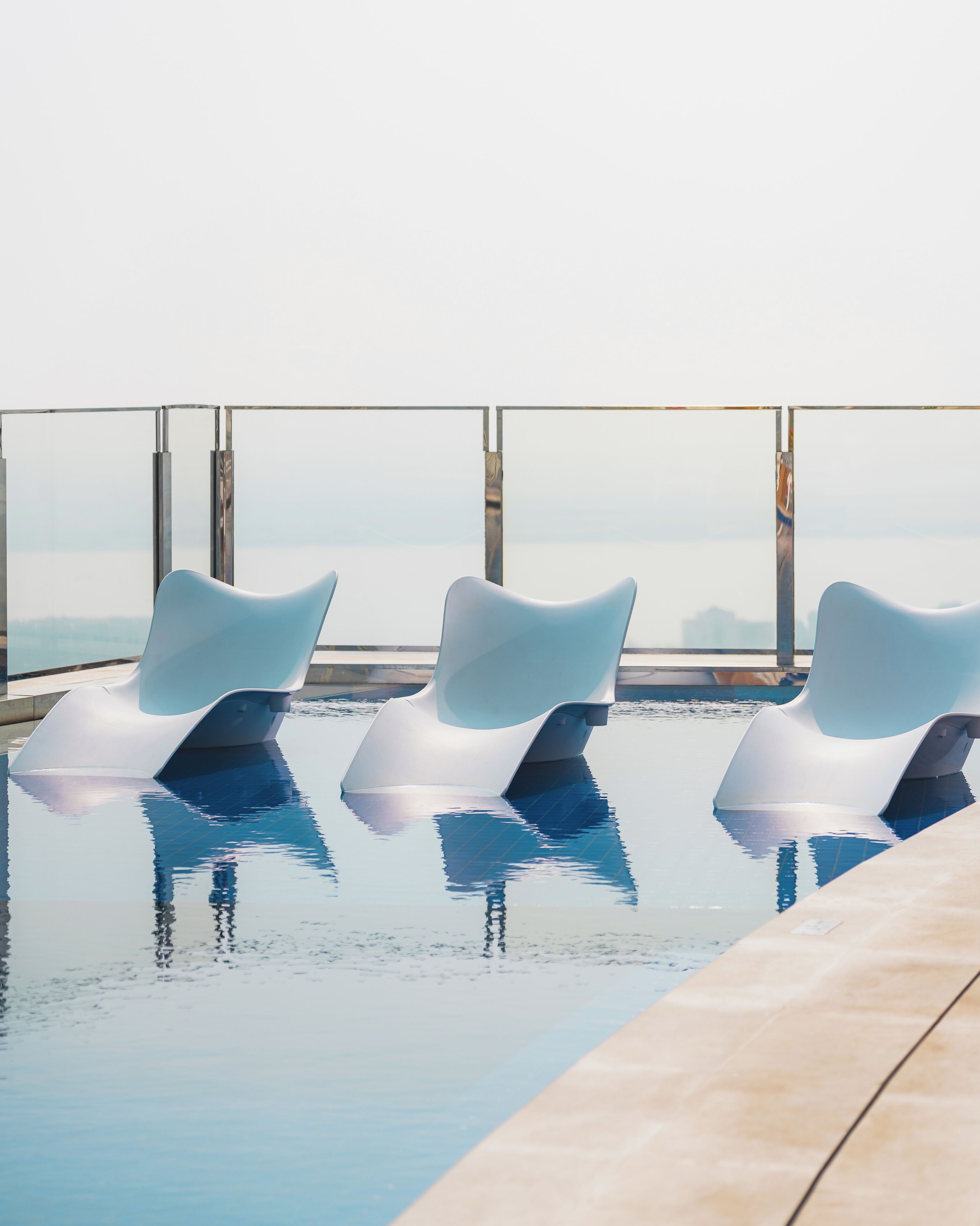 Área da piscina com cadeiras modernas e vista ampla do horizonte.