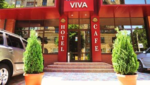 Um edifício com fachada vermelha, uma placa com a inscrição "VIVA HOTEL CAFE" e duas plantas em vasos nos degraus.