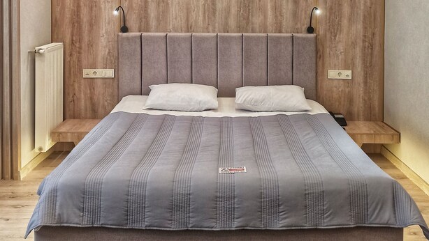 Quarto moderno com parede de painéis de madeira, unidade de ar condicionado central, cama com roupa de cama cinza e luminária no teto.