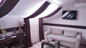 Uma sala de estar com sofá, mesa de centro, escrivaninha e televisão fixada na parede.
