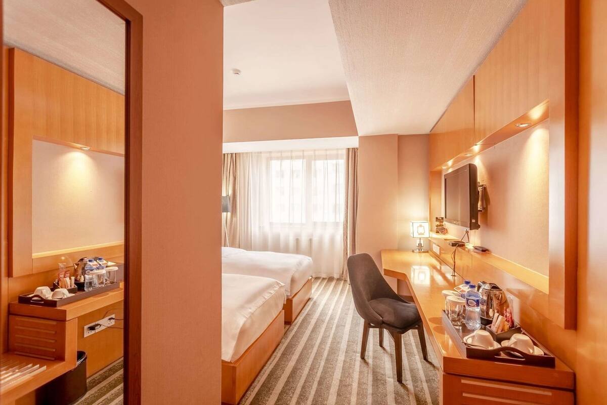 Quarto de hotel com duas camas, uma escrivaninha com cadeira, televisão e minibar.