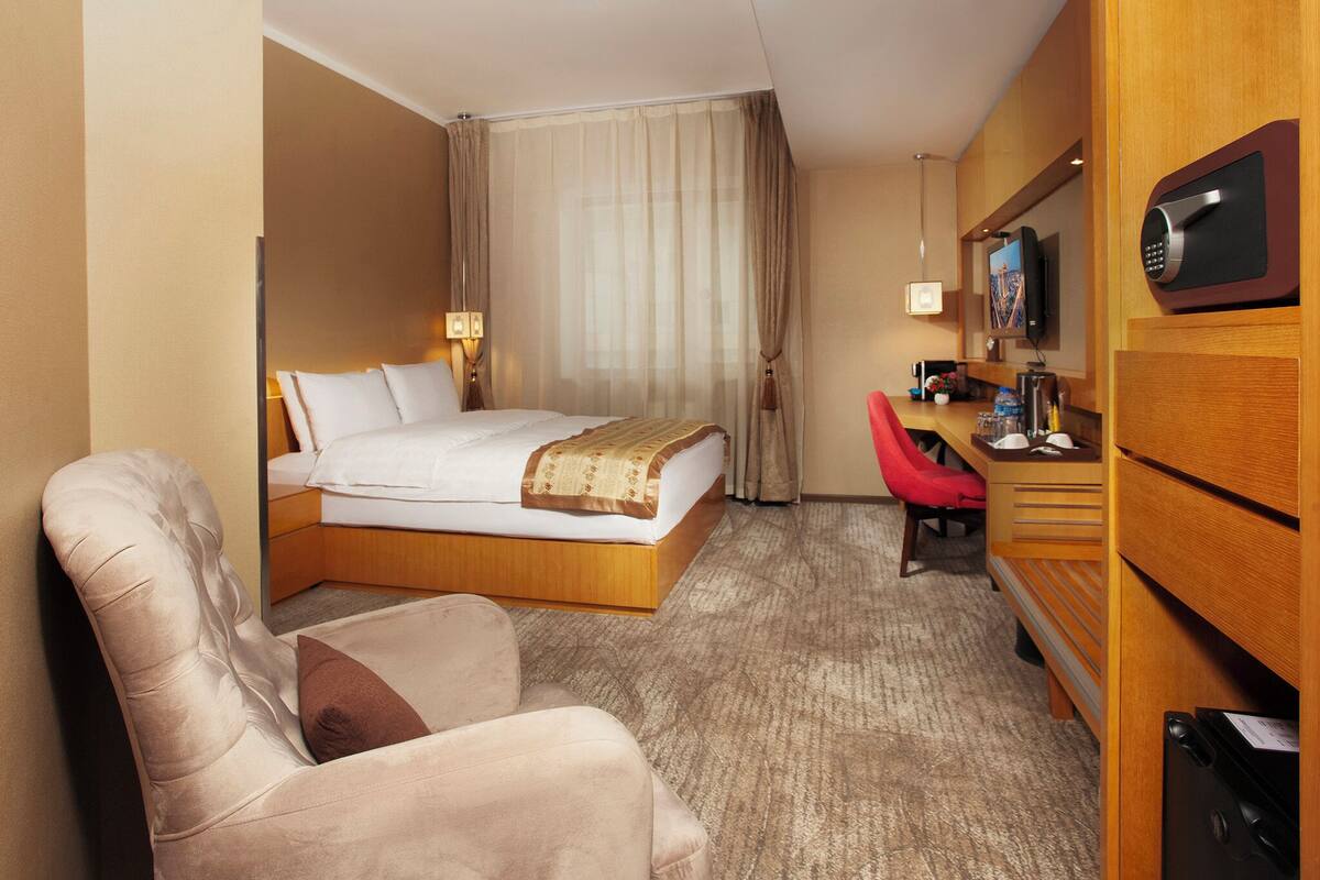 Quarto de hotel com cama, escrivaninha, cadeira, televisão e minibar.