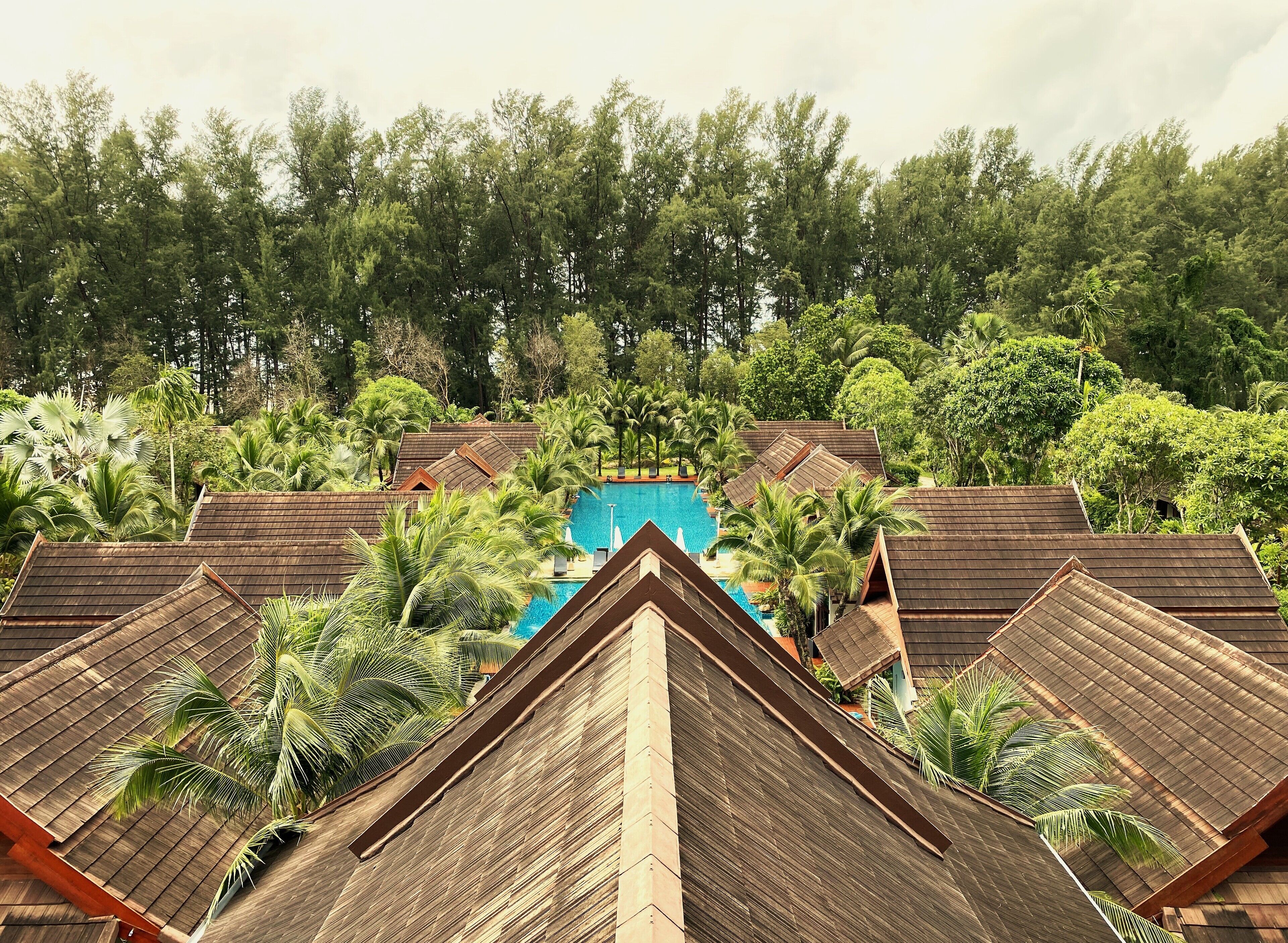 Um resort com vários edifícios de telhado de madeira, uma piscina central e vegetação tropical exuberante.