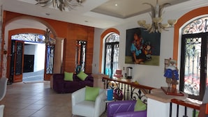 Uma sala de estar espaçosa com um sofá roxo, uma poltrona branca e uma mesa de centro. Há objetos decorativos na mesa de centro e um quadro na parede.
