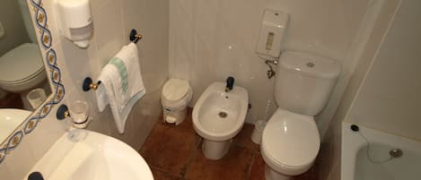 Um banheiro com pia, duas toalhas sanitárias, bidê e banheira.