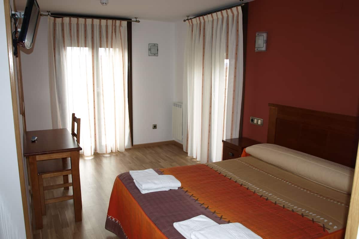 Quarto de hotel com cama, escrivaninha, cadeira e cortinas.