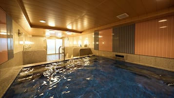 Piscina interior com chão em azulejo, sala de trocas com chuveiro e teto de madeira.