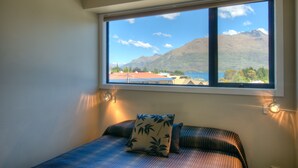 Quarto com uma janela ampla que oferece vista para montanhas e um lago.
