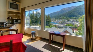 Um quarto com cozinha, uma mesa de jantar com toalha vermelha e vista para uma paisagem montanhosa através de grandes janelas.
