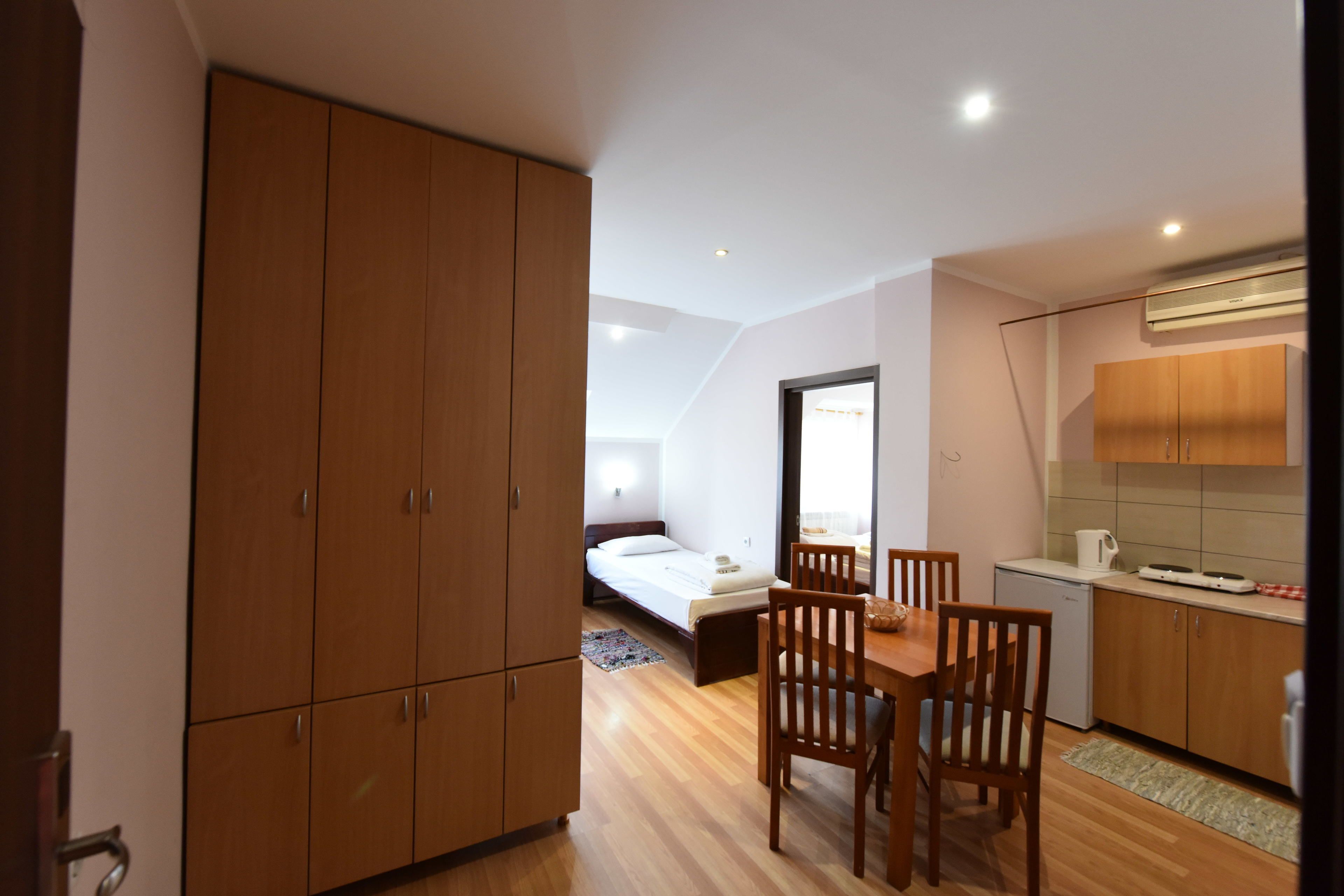 Quarto compacto com cama, guarda-roupa de madeira, mesa de jantar com cadeiras e uma cozinha compacta.