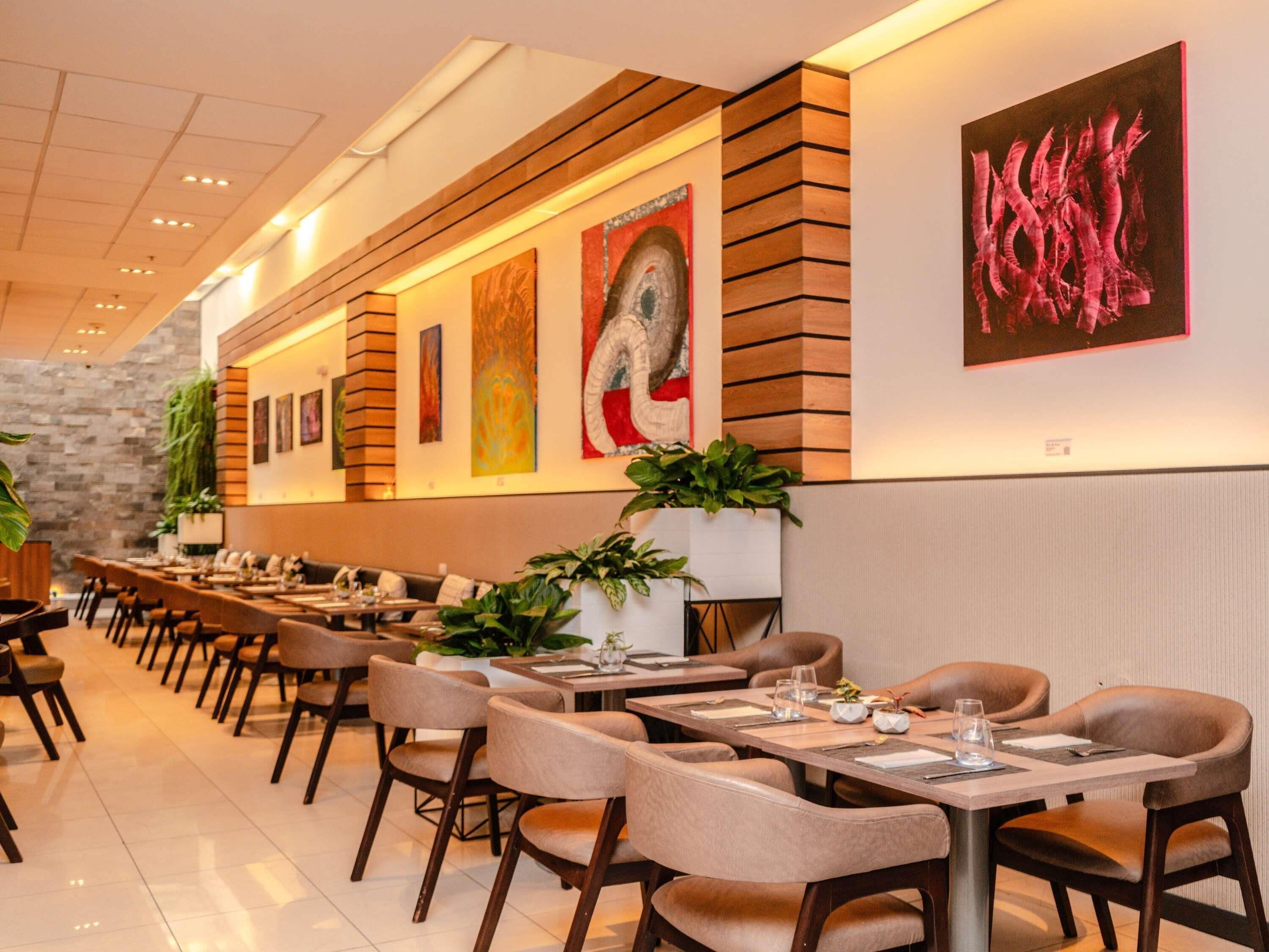 Um restaurante moderno com mesas e cadeiras compridas, uma parede de pedra e obras de arte nas paredes.
