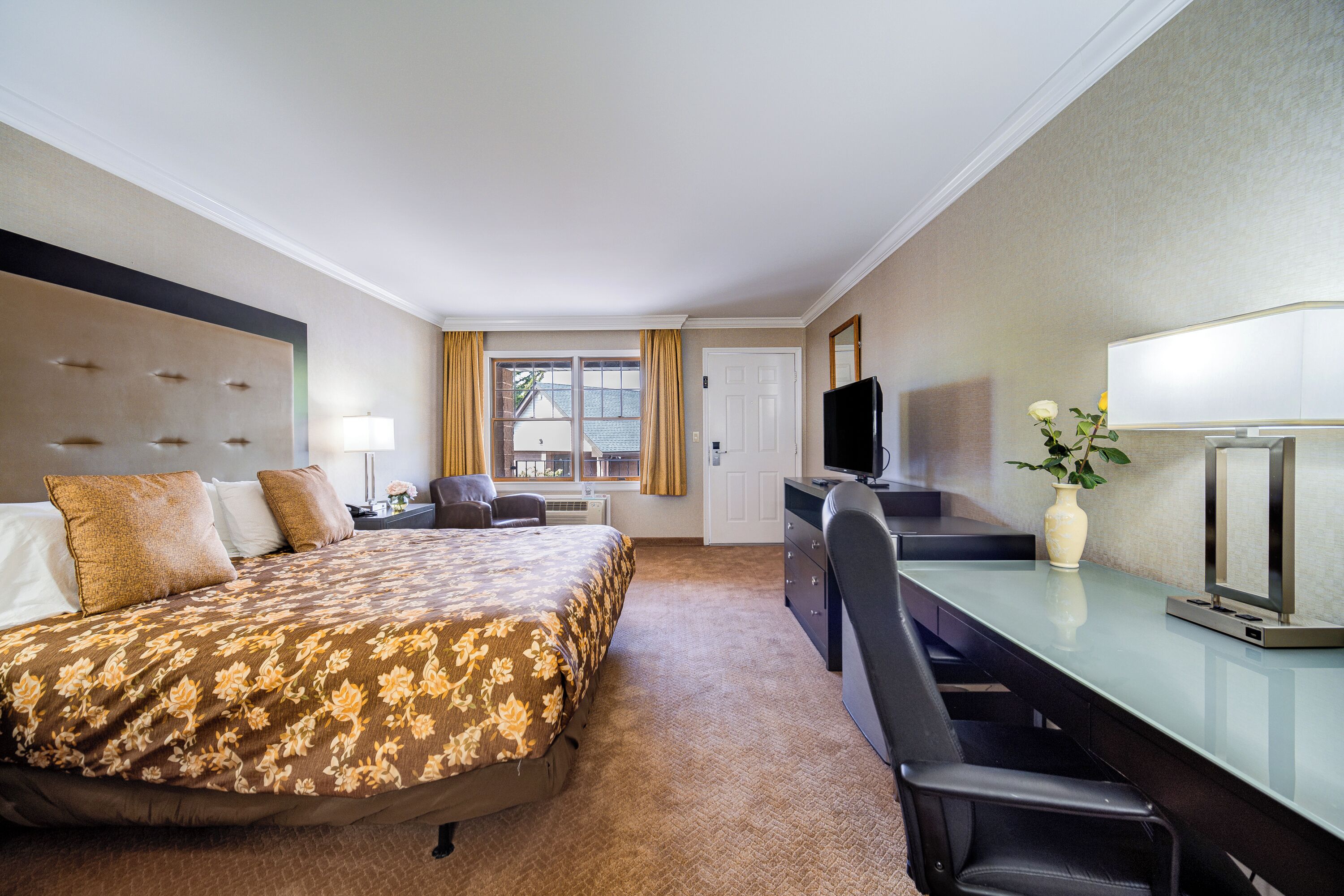 Quarto de hotel com cama grande, escrivaninha, cadeira, televisão e janela com cortinas.