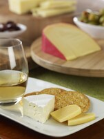 Um prato com queijo, bolachas e um copo de vinho branco sobre uma mesa.