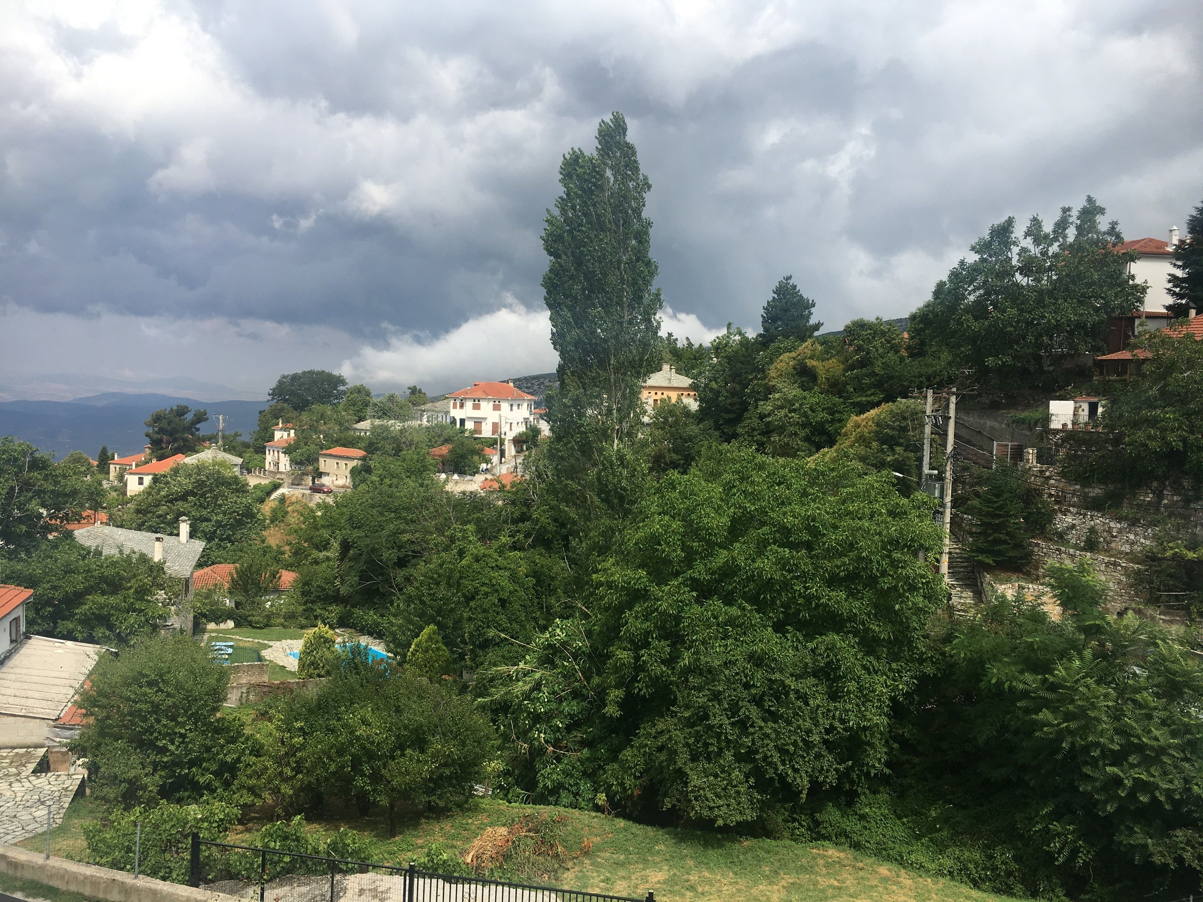 Um bairro residencial numa encosta, com casas, vegetação densa e um céu nublado.