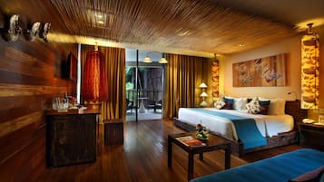 Quarto de hotel com piso de madeira, cama com colcha azul e branca, escrivaninha com luminária e um quadro na parede.