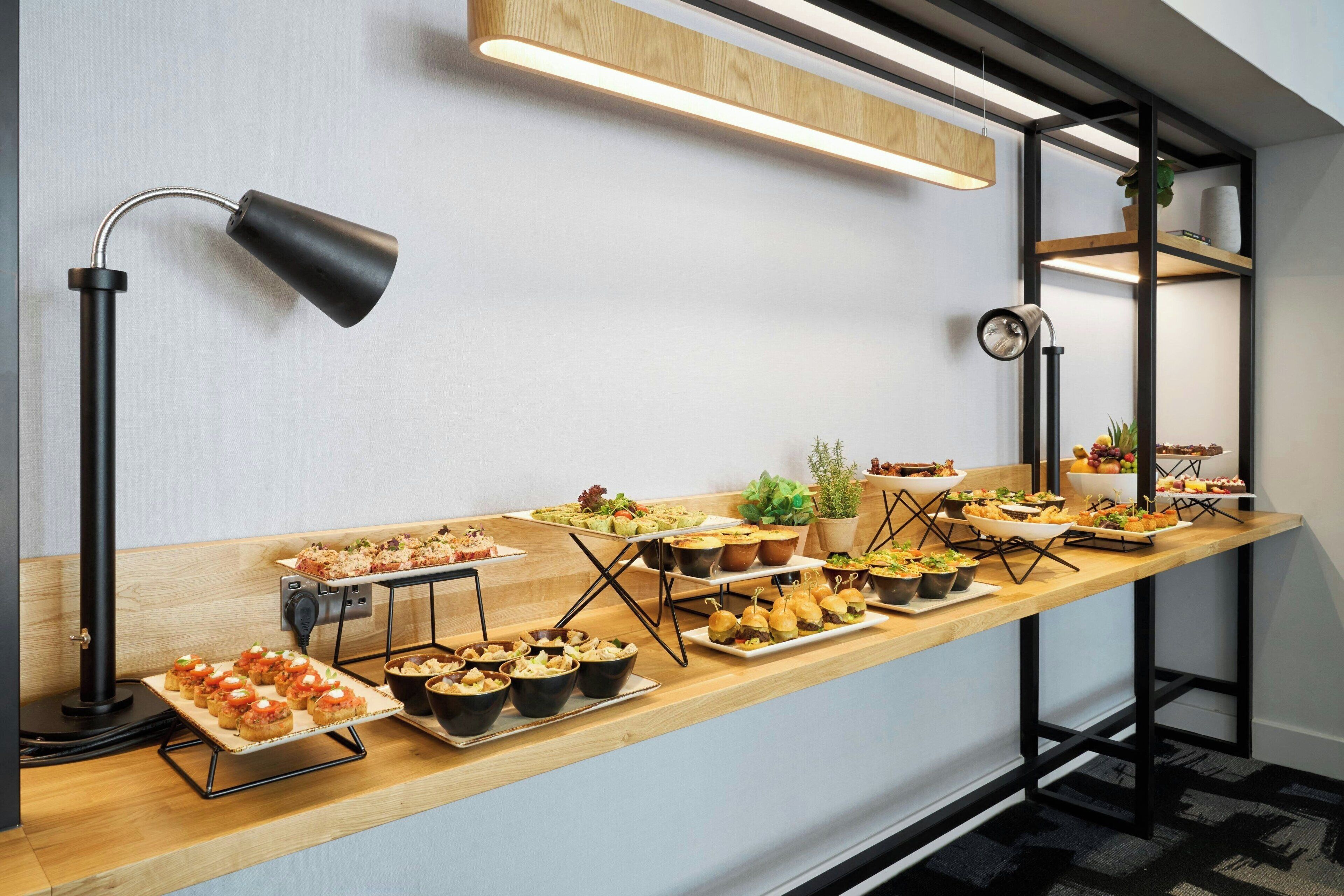 Mesa de buffet com diversos alimentos e iluminação moderna.
